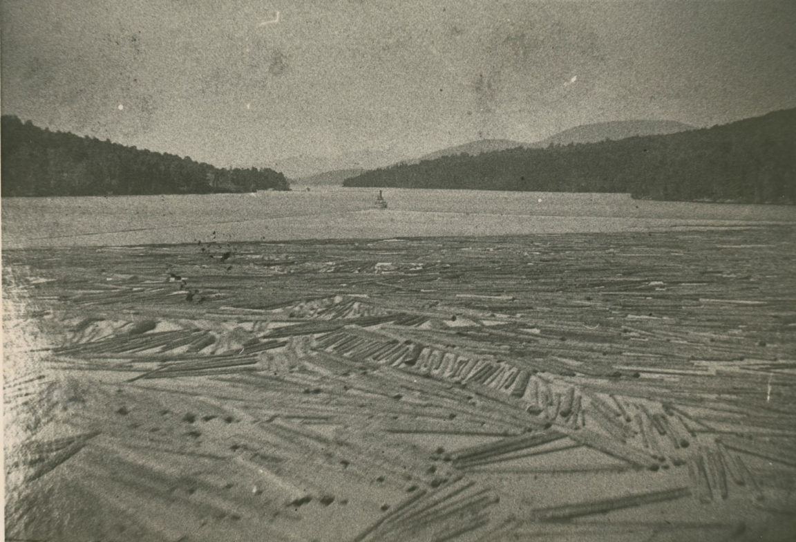 Log boom being towed by steamboat in Long Lake