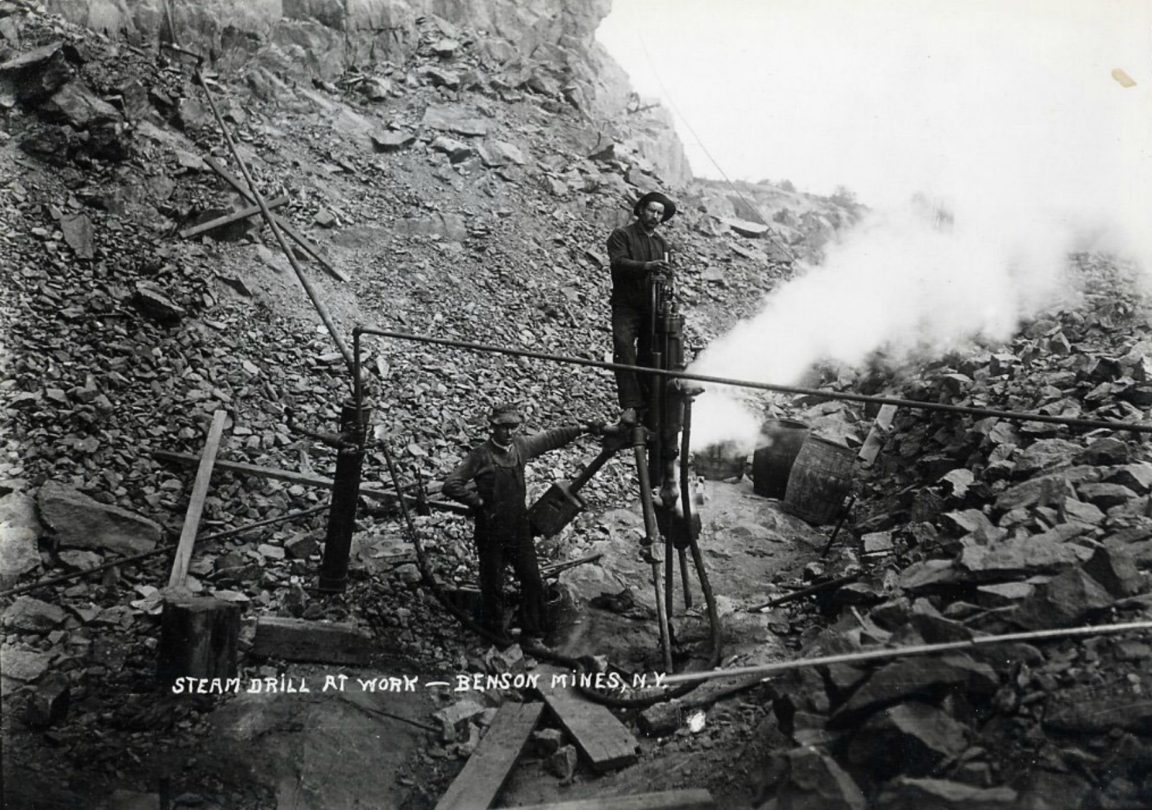 Two miners with a steam drill in the pit at Benson Mines