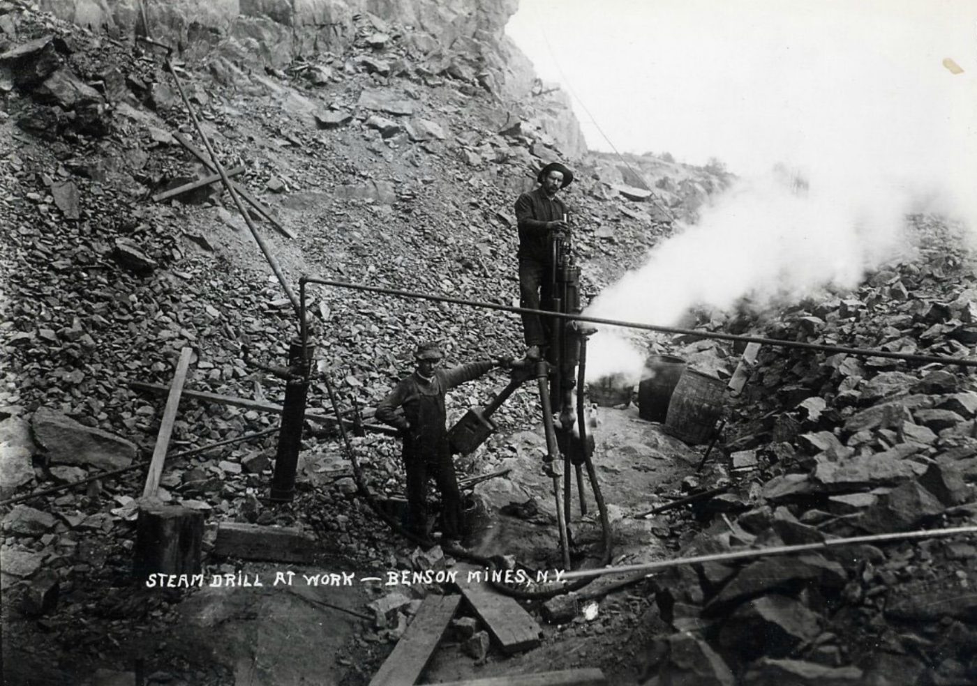 Two miners with a steam drill in the pit at Benson Mines