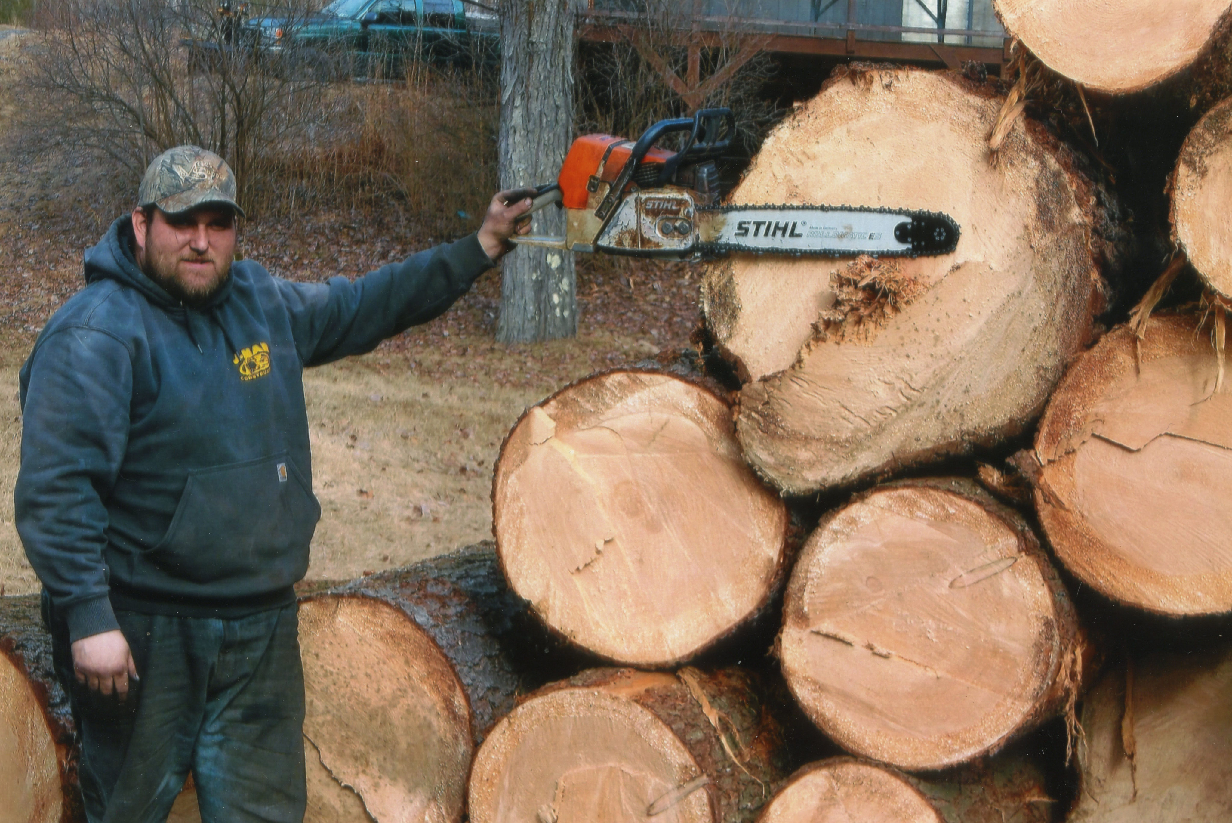 Holding up a chainsaw to a stack of logs in Elizabethtown